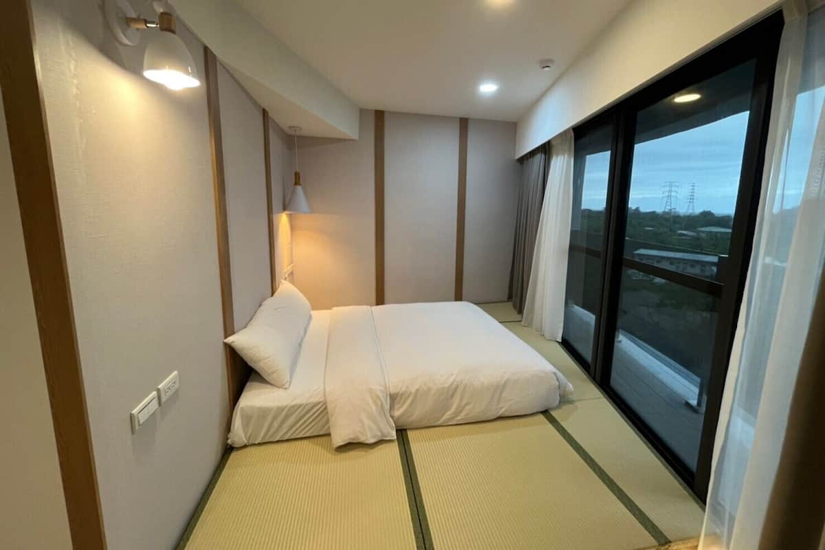 Quarto de hotel com cama, mesa de cabeceira, abajur e uma grande janela com vista.