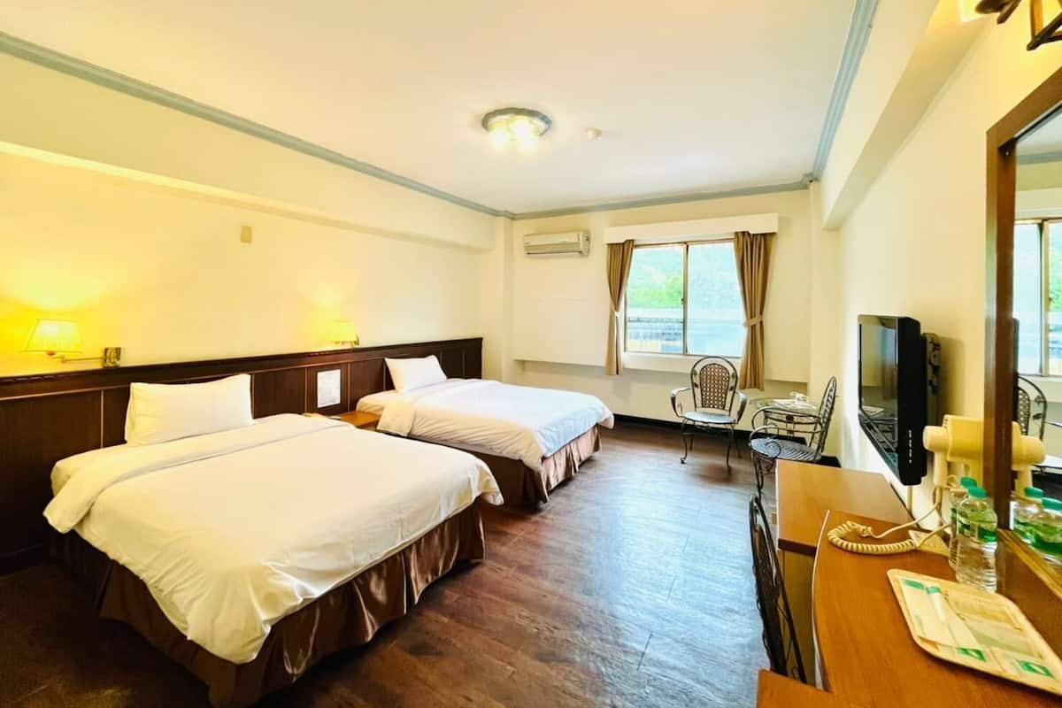 Quarto de hotel com duas camas, uma mesa de trabalho com telefone, uma cadeira e uma televisão.
