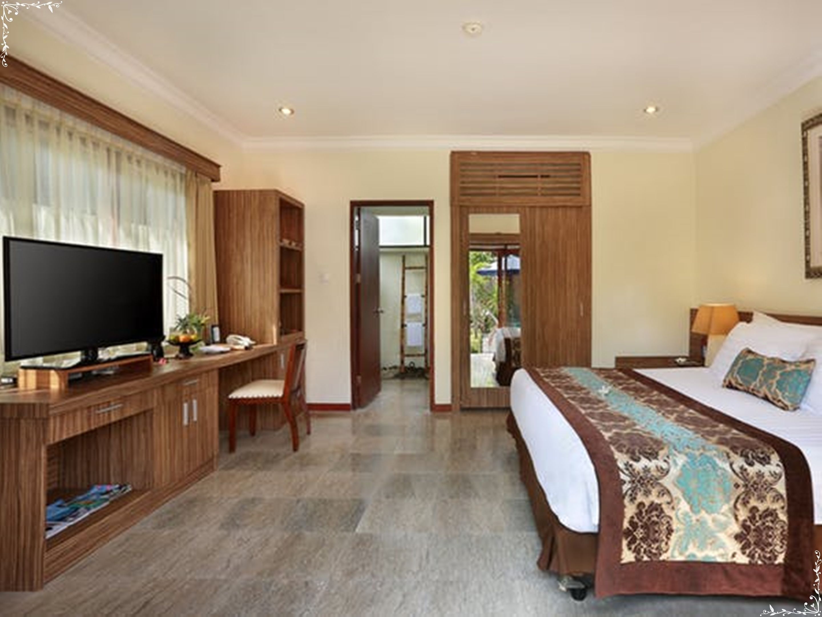 Quarto de hotel com televisão, mobiliário de madeira, cama com roupa de cama estampada e vista para o exterior.