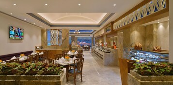 Uma sala de jantar de hotel com paredes de mármore, um balcão central de serviço e disposição de mesas.
