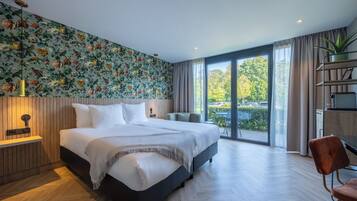 Quarto moderno com uma cama grande, piso de madeira, papel de parede floral e vista para o verde pela janela.