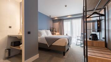 Quarto de hotel moderno com cama, mesa de cabeceira, poltrona, escrivaninha e cabides.