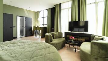 Quarto de hotel com uma cama grande, duas poltronas, uma mesinha com um vaso, televisão e lareira.