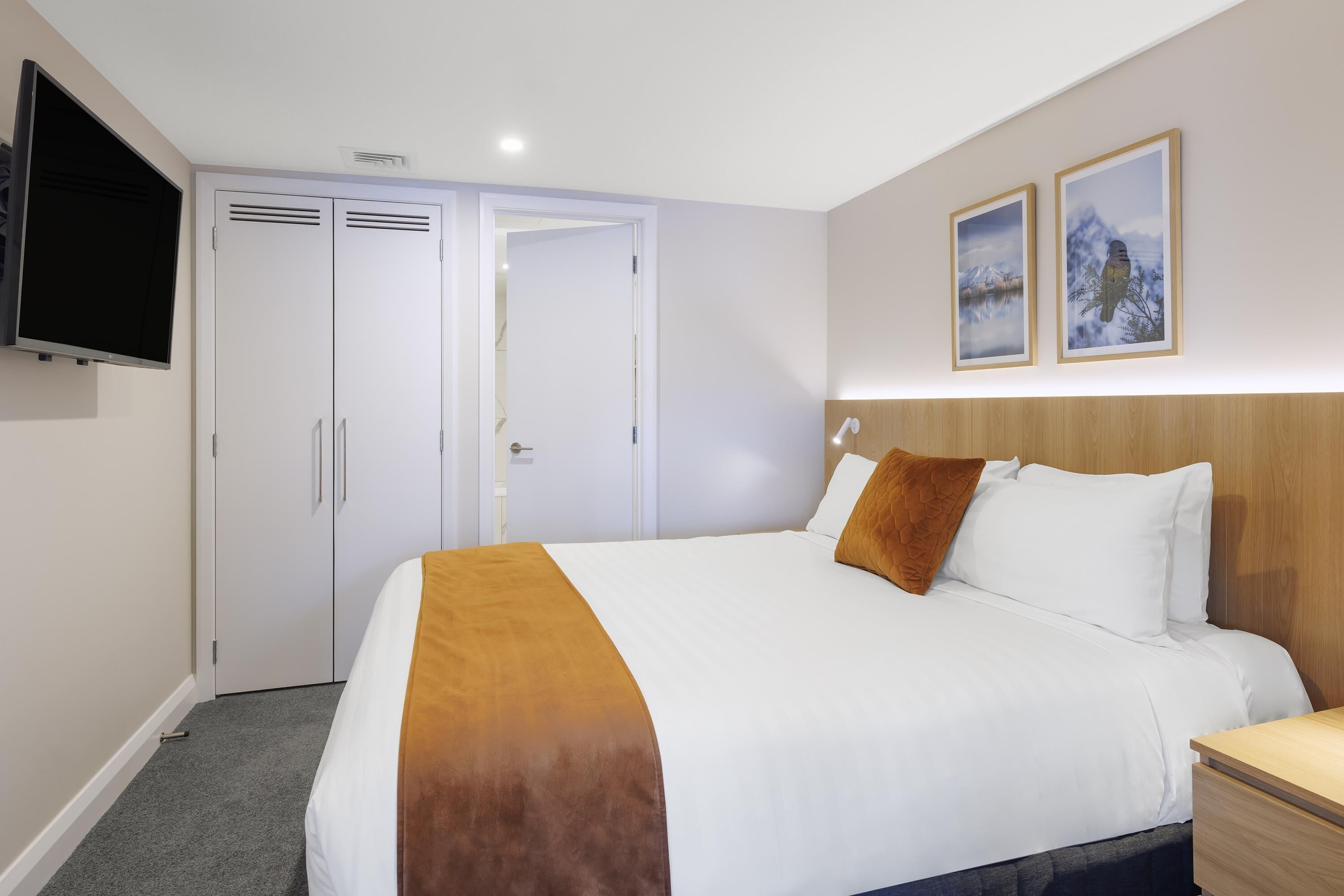 Quarto de hotel com cama, mesa de cabeceira, armário e televisão fixada na parede.