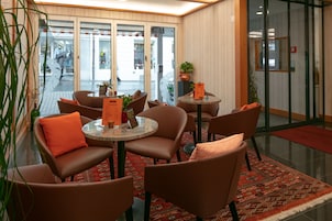 Um hall de entrada com mesas e cadeiras redondas, um tapete estampado e plantas em vasos.