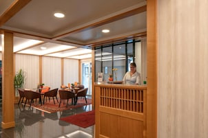 Um saguão de hotel com balcão de recepção, área de estar e uma grande janela.