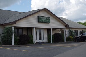 Edifício do Shiretown Inn & Suites com uma placa, um estacionamento e um veículo na frente.