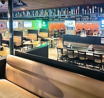 Um restaurante com cabines e mesas, uma área de bar com diversas torneiras de cerveja e um cardápio em lousa.