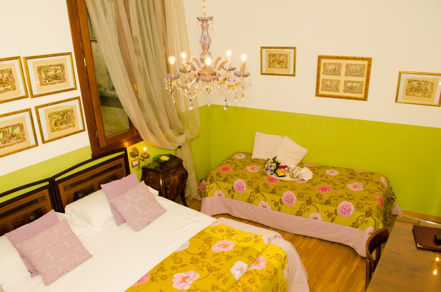 Quarto de hotel com duas camas, um candelabro e quadros nas paredes.