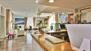 Uma área de recepção de hotel com um balcão de madeira, um computador e um mapa na parede.