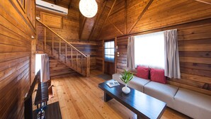 Interior de uma cabana de madeira com escadas, um sofá, uma mesa e um lustre.