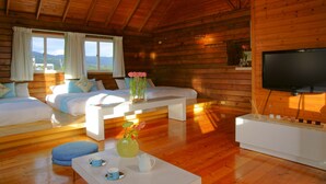 Uma cabana acolhedora com paredes de madeira, uma cama grande, um sofá, uma TV e vista para as montanhas pelas janelas.
