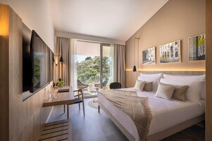 Quarto de hotel moderno com uma cama grande, uma escrivaninha e uma varanda com vista para o verde.