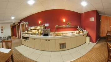 Uma área de buffet com um balcão curvo, uma parede vermelha e piso ladrilhado.
