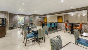 Uma sala de jantar ampla com várias mesas e cadeiras, um balcão e vista para o exterior através de grandes janelas.