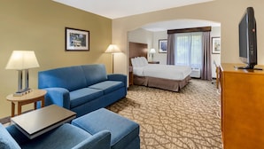 Quarto de hotel com sofá azul, uma cama, televisão e uma mesinha.
