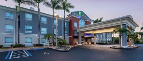 Um hotel Holiday Inn Express com design moderno, que apresenta um amplo estacionamento, palmeiras e uma entrada bem iluminada.