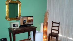 Um quarto com televisão sobre mesa de madeira, radiador branco, cesto de vime e cadeira de madeira.