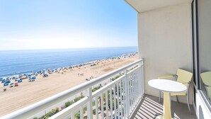 Uma varanda com vista para a praia, uma mesa pequena e uma cadeira.