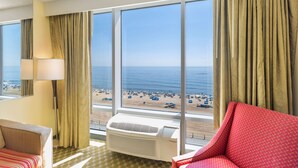 Quarto de hotel com uma janela grande que oferece vista para a praia e o oceano.