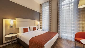 Quarto de hotel com cama grande, mesa de cabeceira, cadeira e abajur.