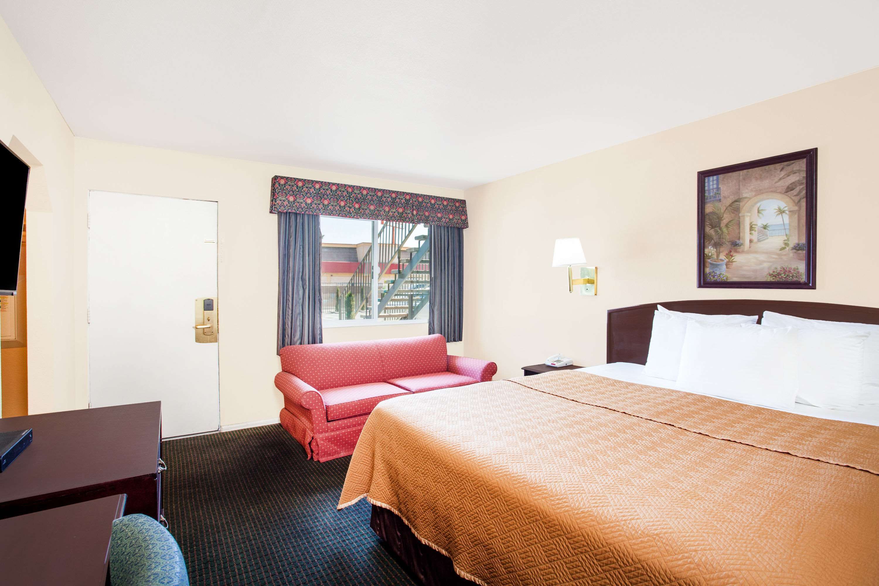 Quarto de hotel com uma cama, um sofá vermelho, uma escrivaninha e um quadro na parede.