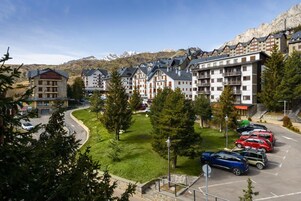Um hotel com vários andares, estacionamento e montanhas ao fundo.