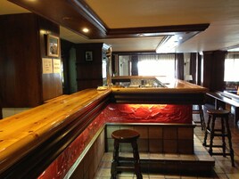 Uma área de bar com balcão de madeira, banquetas e um espaço de estar acolchoado em vermelho.