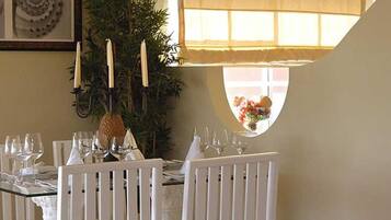 Mesa de jantar posta com cadeiras brancas, candelabro e copos de vinho.