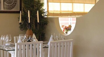 Mesa de jantar posta com cadeiras brancas, candelabro e copos de vinho.