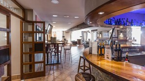 Uma área de bar com balcão de madeira, banquetas e variedade de garrafas.