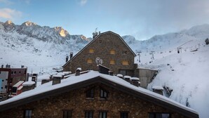 Um edifício de pedra com telhado inclinado, rodeado por montanhas cobertas de neve e um teleférico ao fundo.