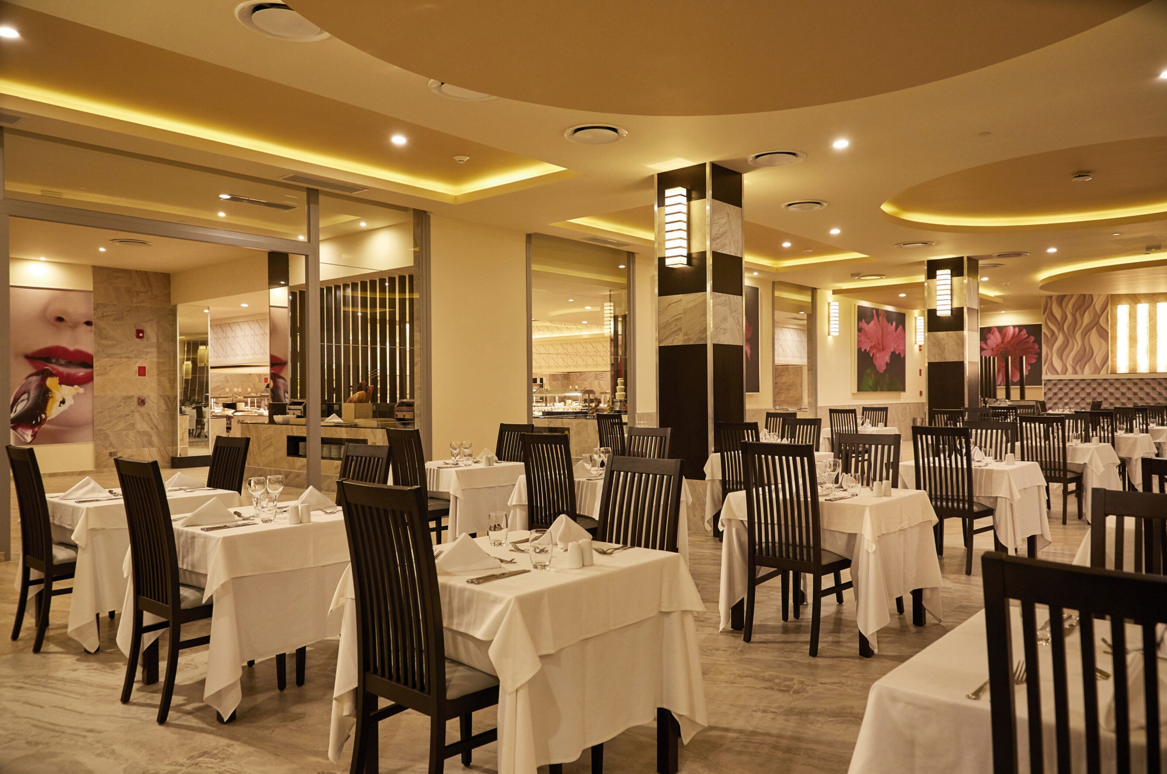 Um restaurante com várias mesas e cadeiras, bem iluminado por luzes no teto, e um design de interiores moderno.