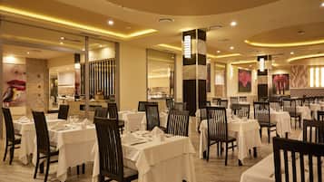 Um restaurante com várias mesas e cadeiras, bem iluminado por luzes no teto, e um design de interiores moderno.