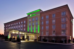 Um hotel Holiday Inn de vários andares, com um letreiro verde chamativo, entrada coberta e estacionamento.