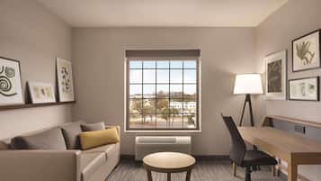 Quarto de hotel com sofá, mesa redonda, escrivaninha e janela com vista para edifícios.