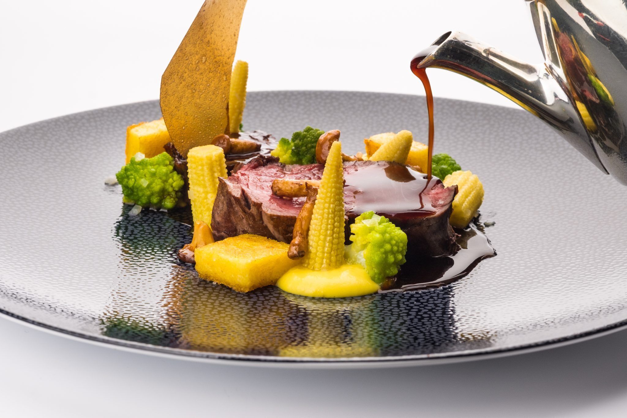 Um prato de comida com diversos legumes e um pedaço de carne, com molho sendo adicionado.