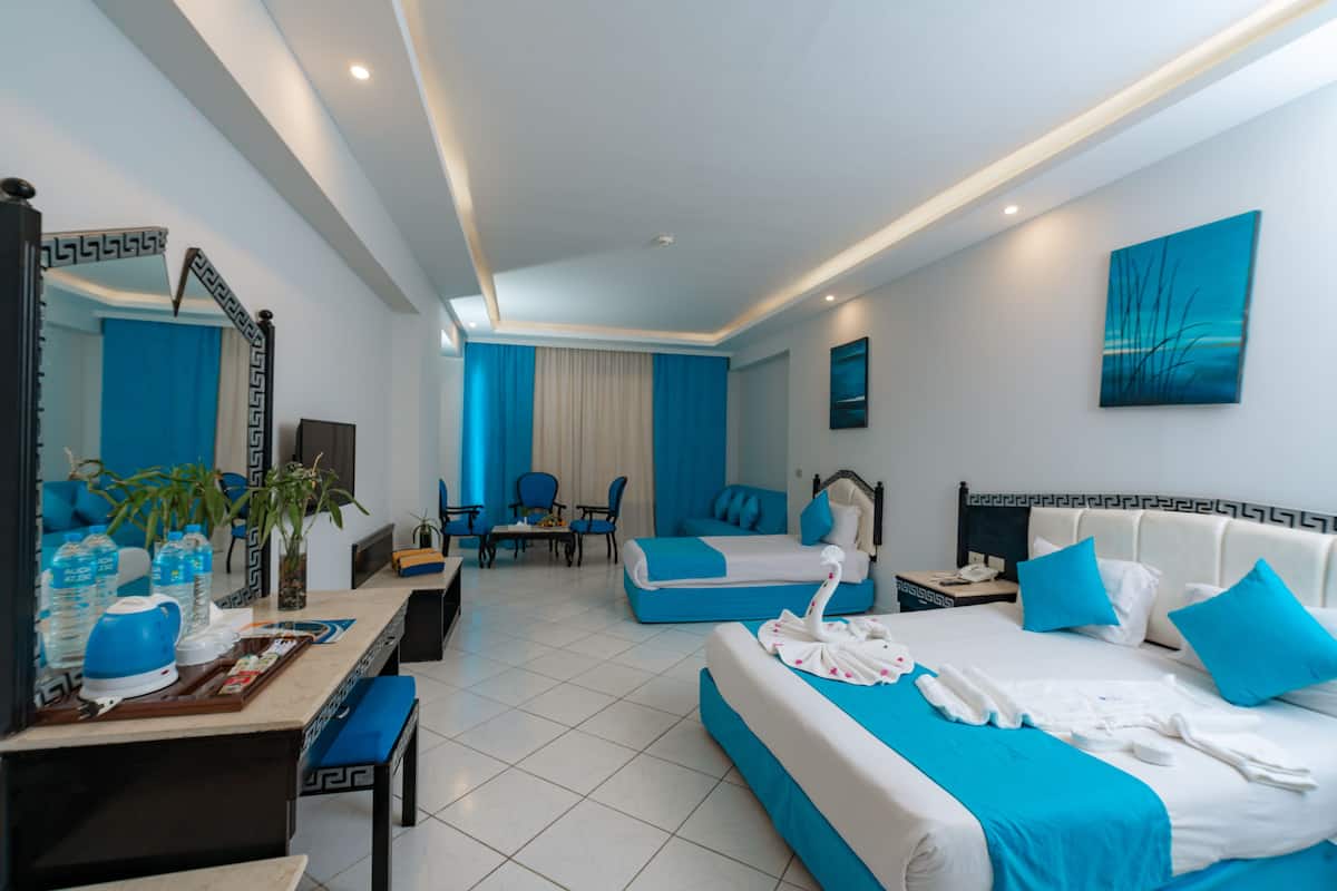 Quarto de hotel moderno com uma cama grande, uma escrivaninha com cadeira, uma mesa de jantar com cadeiras e uma janela grande com cortinas.