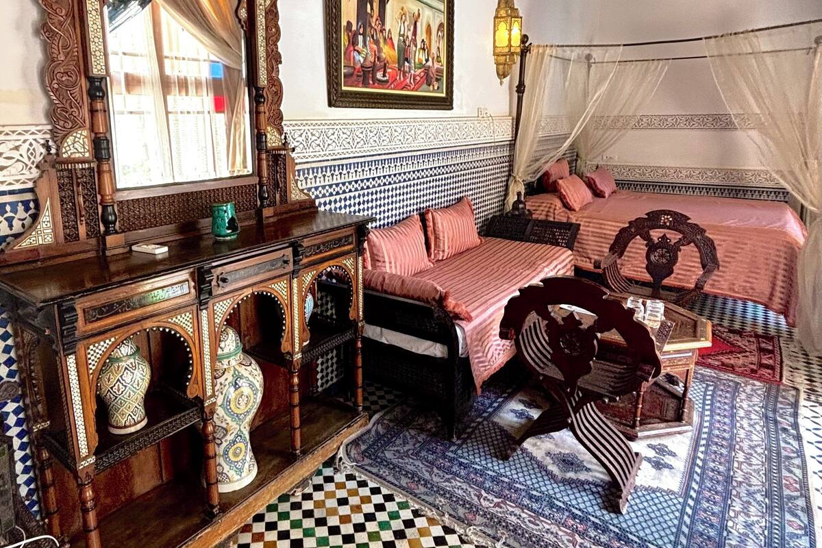 Um quarto tradicional marroquino com piso xadrez, móveis ornamentados, um espelho grande, um quadro e uma cama com dossel.