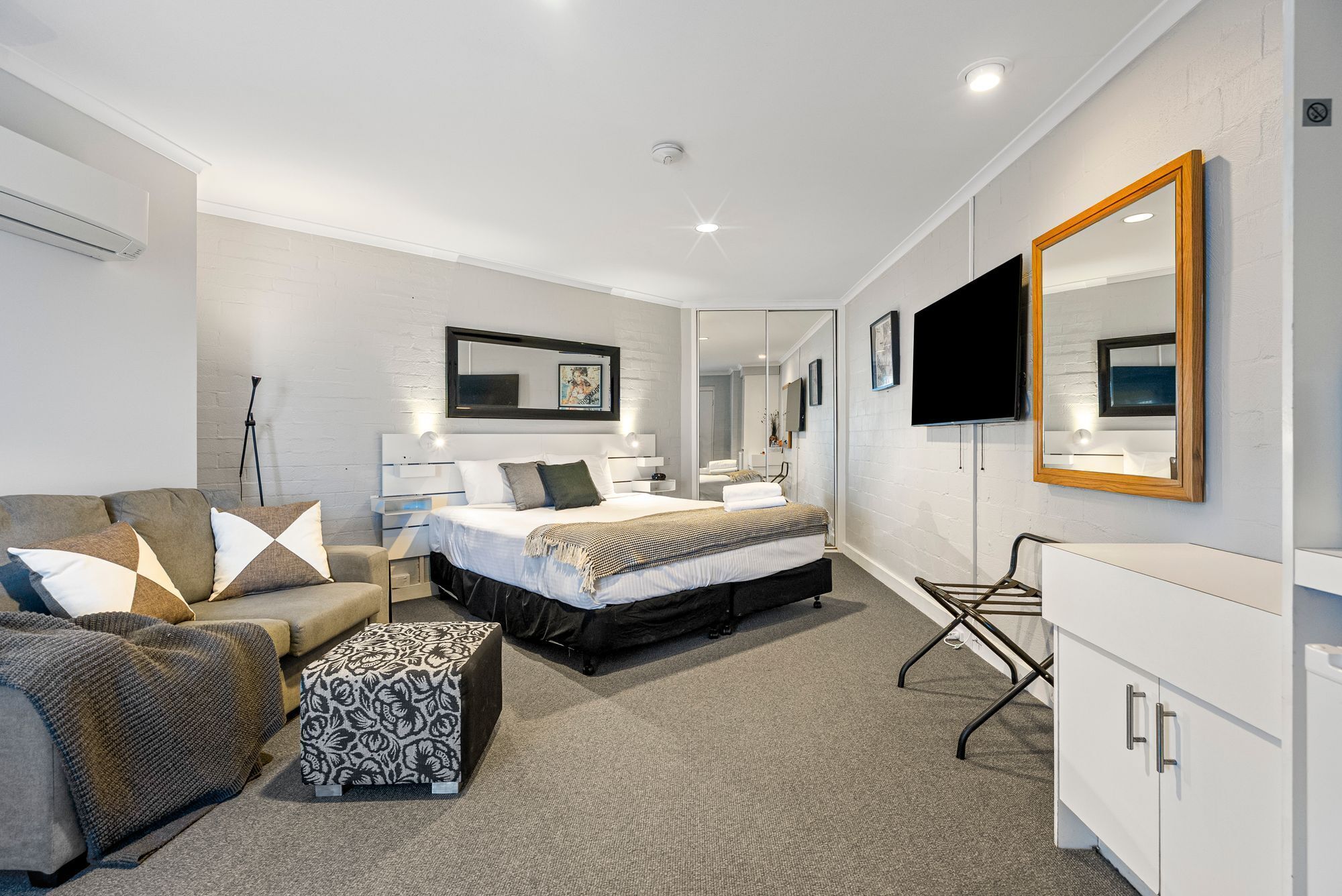 Quarto moderno com cama, sofá, televisão e espelho.