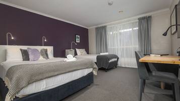 Quarto de hotel com duas camas, uma escrivaninha e uma cadeira.