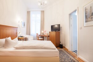 Quarto de hotel com uma cama grande, uma escrivaninha com cadeira, televisão e um quadro na parede.