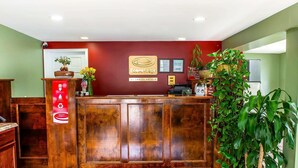 Bancada de recepção com tapete vermelho, placa da EconoLodge e uma grande planta em vaso.