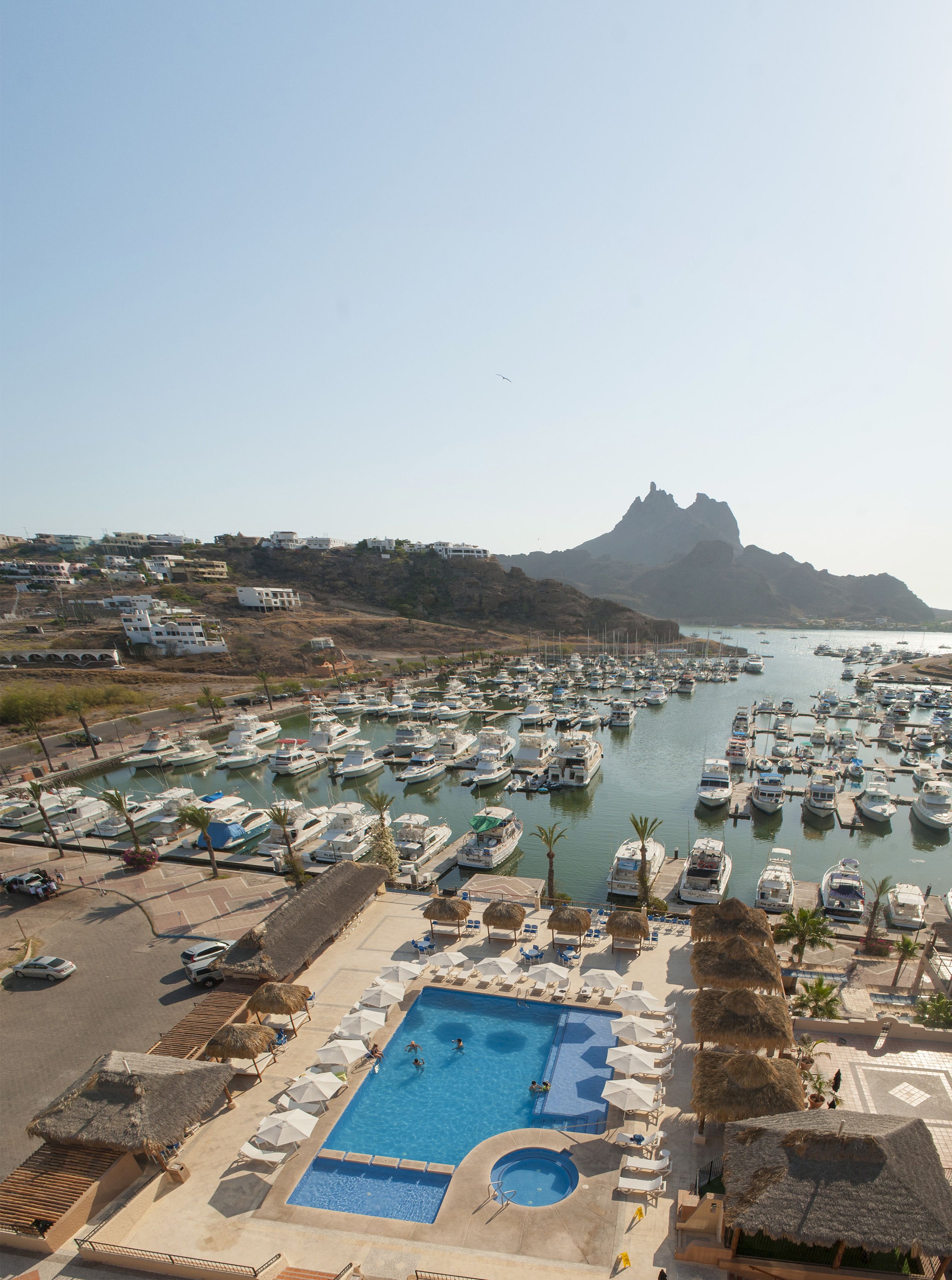 Uma marina com vários barcos atracados, uma piscina com espreguiçadeiras e uma montanha ao fundo.