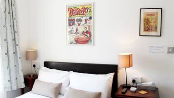 Quarto de hotel com uma cama, duas mesas de cabeceira, um criado-mudo, uma luminária, um cartaz emoldurado na parede e uma cortina.