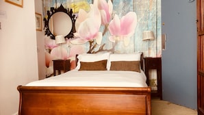 Quarto com cama grande, cabeceira de madeira, painel floral na parede, espelho e porta com o número 3.