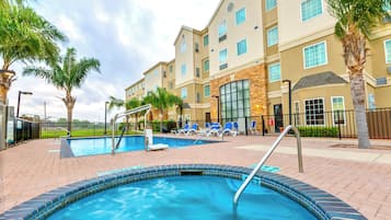 Um hotel com piscina, palmeiras e um pátio de tijolos.