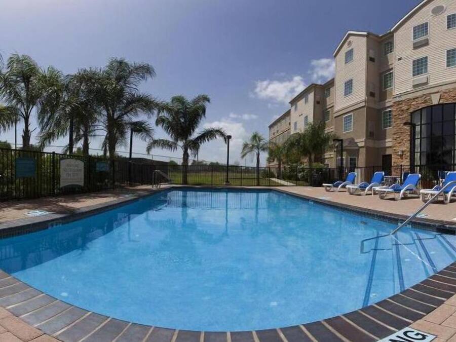 Piscina com espreguiçadeiras, palmeiras e um edifício com detalhes em pedra.