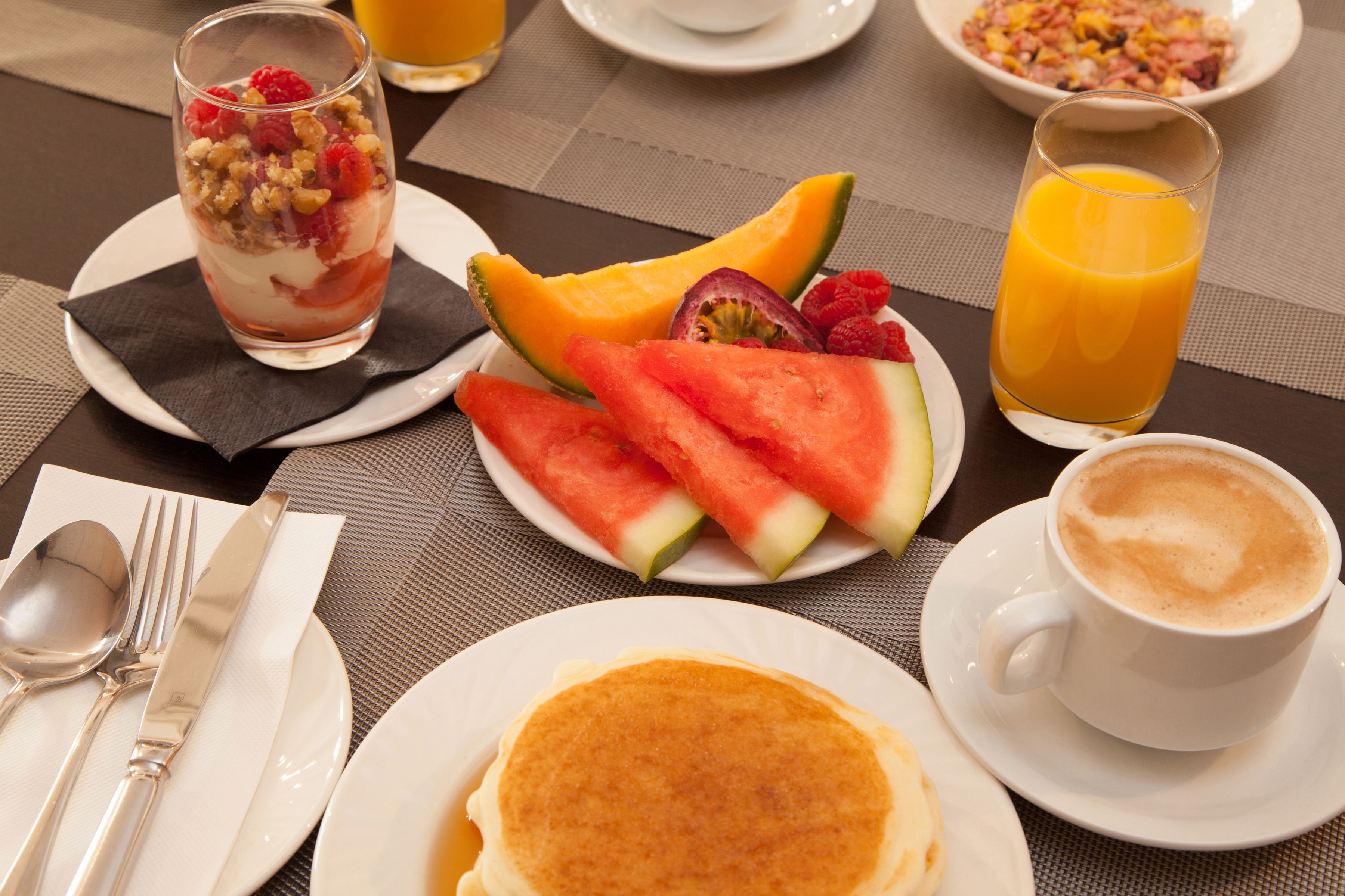 Mesa de café da manhã com panquecas, frutas e um copo de suco de laranja.