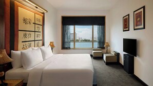 Quarto de hotel com uma cama grande, escrivaninha, cadeira, televisão e janela com vista para a paisagem urbana.